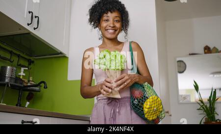 African American woman holds lettuce and mesh bag with fresh vegetables ...