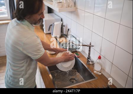 Bearded man washing dishes in his home kitchen. Householder concept ...