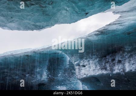 Clean water falling from fragile transparent icicles into blue stream ...