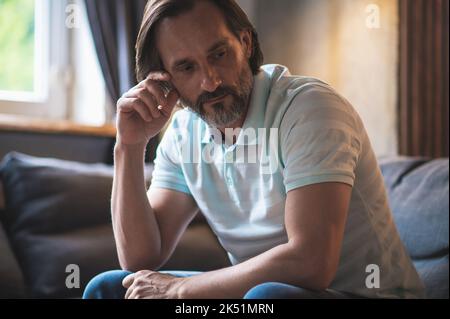 Stressed mature bearded man sitting on a chair with hand on head ...