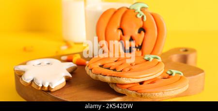 Board with Halloween cookies, candy corns and glass of milk on yellow ...