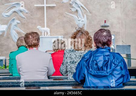People praying on pews at Knock Shrine, a wall on which the apparitions ...