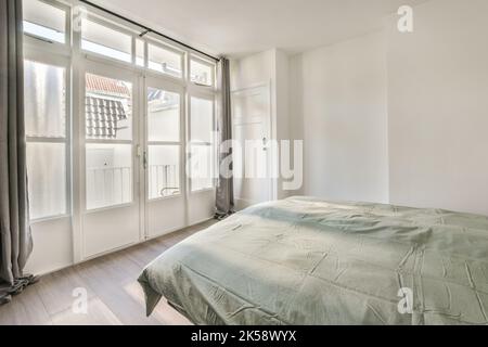 Comfortable bed located near balcony door with curtains in cozy light ...