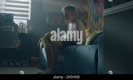 A teenager boy applying bandage to his bruised knee. Sitting on the bed ...