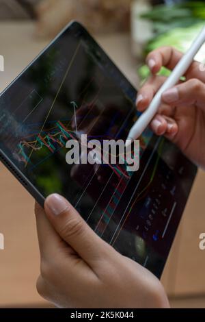 young woman, watching the stock market on her tablet, while drawing on ...