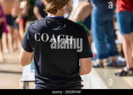 Back view of swimming coaches, wearing COACH shirt, working at an ...