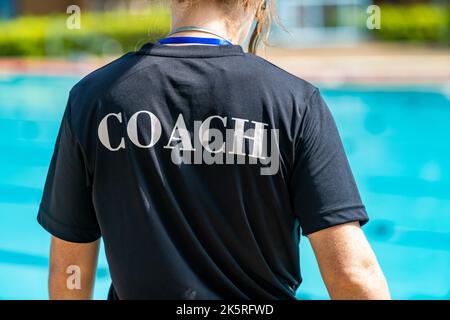 Back view of female swimming coaches, wearing COACH shirt, working at ...