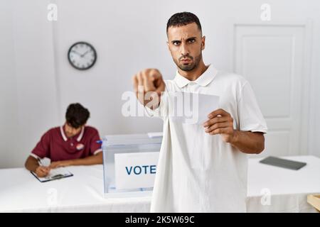 Young hispanic man voting putting envelop in ballot box surprised with ...