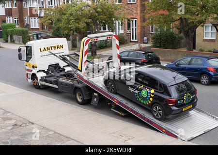 break-down zipcar car is hoisted onto a loading ramp and secured on a ...