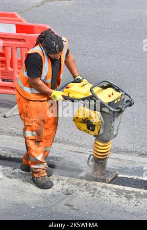 Worker is using vibrating plate compactor for ground road compaction ...