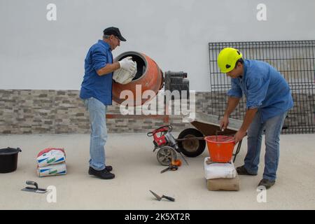 An elderly bricklayer and a young one are mixing concrete with a ...