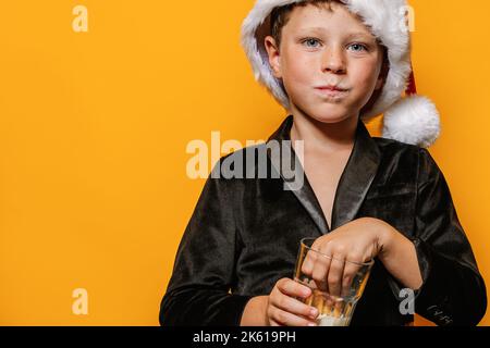Funny boy in stylish black jacket and Santa hat looking at camera while ...
