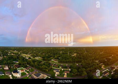 Colorful round rainbow over rural town suburbs against blue evening sky ...