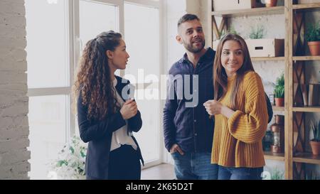 Confident realtor is describing advantages of new house to young couple ...