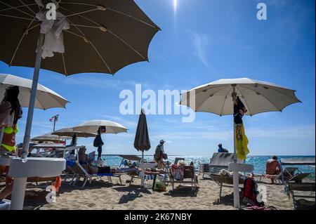 Sunbathers and beachgoers with sunbeds and parasols on Sottovento beach ...