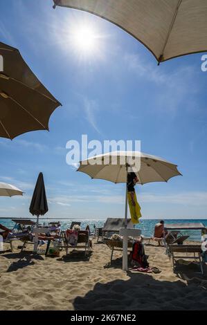 Sunbathers and beachgoers with sunbeds and parasols on Sottovento beach ...