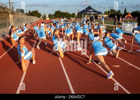 Blue-uniformed multiracial high school cheerleaders exercise to limber ...