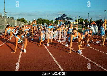 Blue-uniformed multiracial high school cheerleaders exercise to limber ...