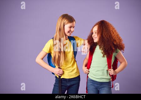 Studio Shot Of Two Girls With Backpacks Going To School On Purple ...