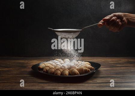 Womens hands sprinkle powdered sugar through a sieve on freshly baked ...