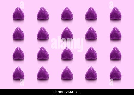 A repeating pattern of heart-shaped candies wrapped in purple foil on a ...