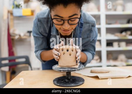 Smiling man forming clay sculpture near blurred african american ...