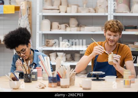 Interracial couple in aprons painting on clay sculptures during date in ...