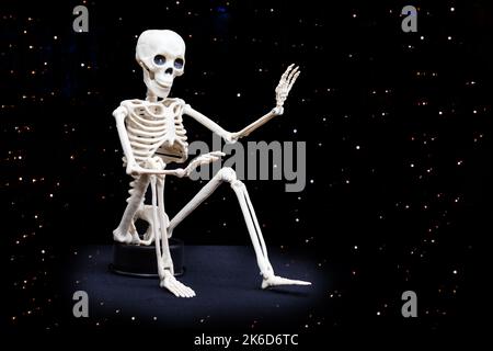 A fake human skeleton sitting on a black background and pointing with ...