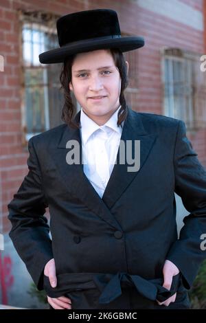 Posed portrait of a hasidic boy with long peyot and a smile. In ...