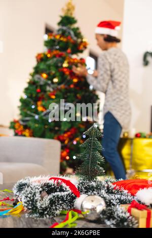 Happy biracial man wearing santa claus hat, decorating christmas tree ...
