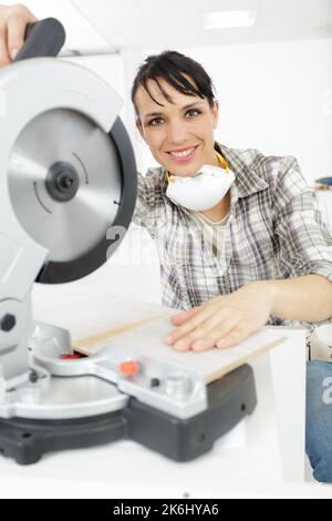 Young woman using a circular saw on a construction site with hard hat ...