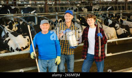 Three cheerful friendly livestock farm workers posing in cowshed Stock ...