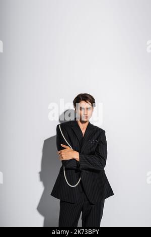 brunette man in trendy blazer with pearls posing while looking at ...