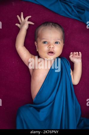 newly born baby laying on red velvet cloth with cute facial expression ...