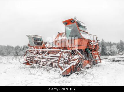 Red broken frozen combine harvester on a snow-covered field. Old broken ...