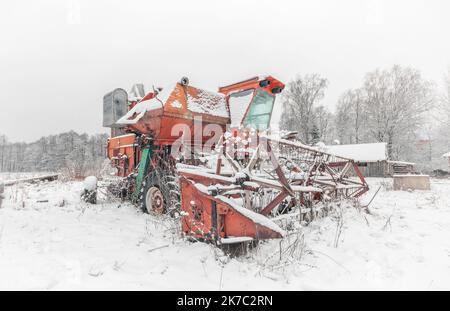 Red broken frozen combine harvester on a snow-covered field. Old broken ...