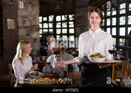 Professional waitress greeting customers at table in rustic restaurant ...