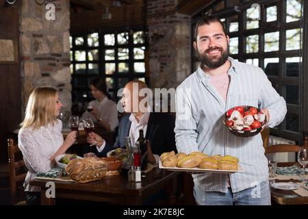 Positive male waiter welcoming guests to country restaurant Stock Photo ...