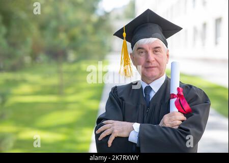 Portrait of an elderly man in a graduation gown and with a diploma in ...