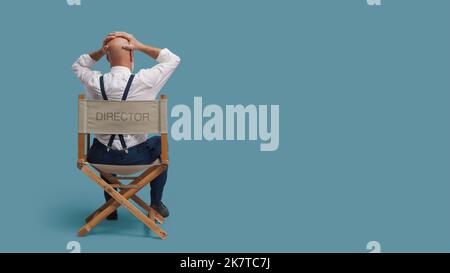 Desperate stressed film director with head in hands, he is sitting on ...