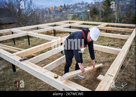 Men workers building wooden frame house on pile foundation. Carpenters installing wooden board ...