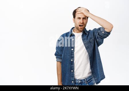 Upset young man slaps his forehead and looks devestated, frustrated by ...