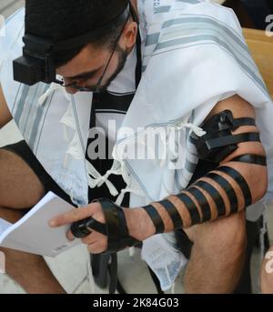 A praying young man with a tefillin on his arm and head, holding a ...