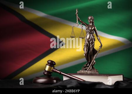 Guyana flag with statue of lady justice and judicial scales in dark ...