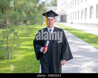 Serious old man in graduation gown holding diploma outdoors Stock Photo ...