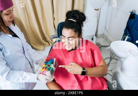 Dental patient choosing dental braces, Patient with dentist choosing colored rubber band ...