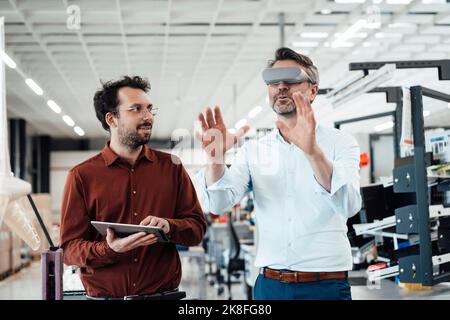Businessman with colleague wearing virtual reality simulator gesturing ...