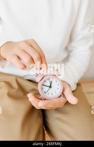 Female hands with alarm clock in bedroom, closeup. Daylight saving time ...