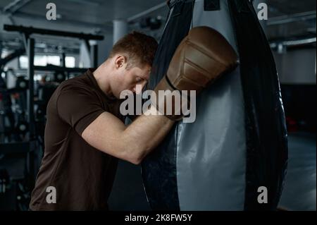 Tired boxer holding punching bag feeling heavy fatigue Stock Photo - Alamy