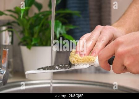 A man washes a sharp steel dirty kitchen knife with a sponge with ...